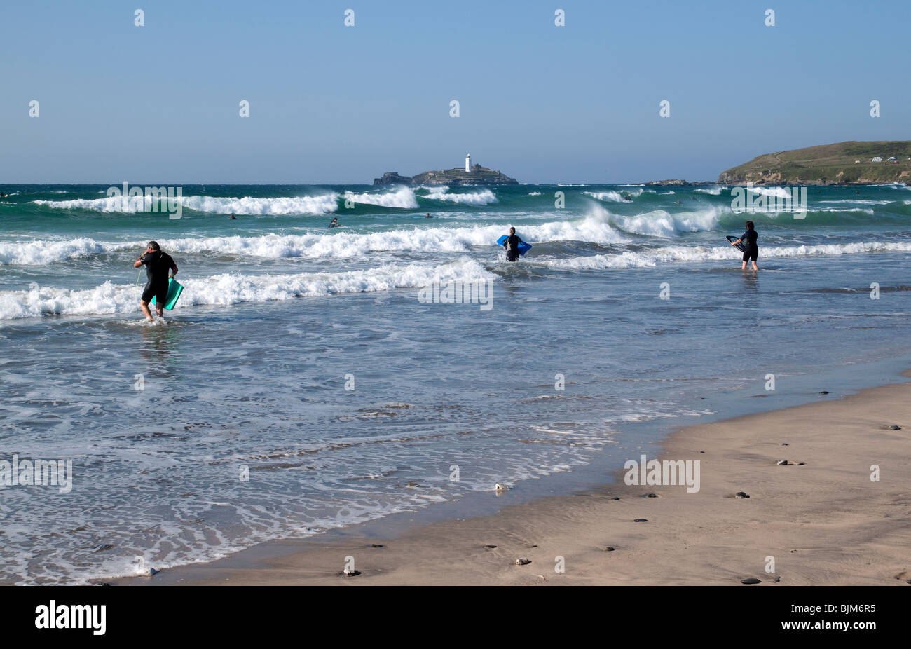 Body boarders entering the sea from Gwithian beach with Godrevy ...