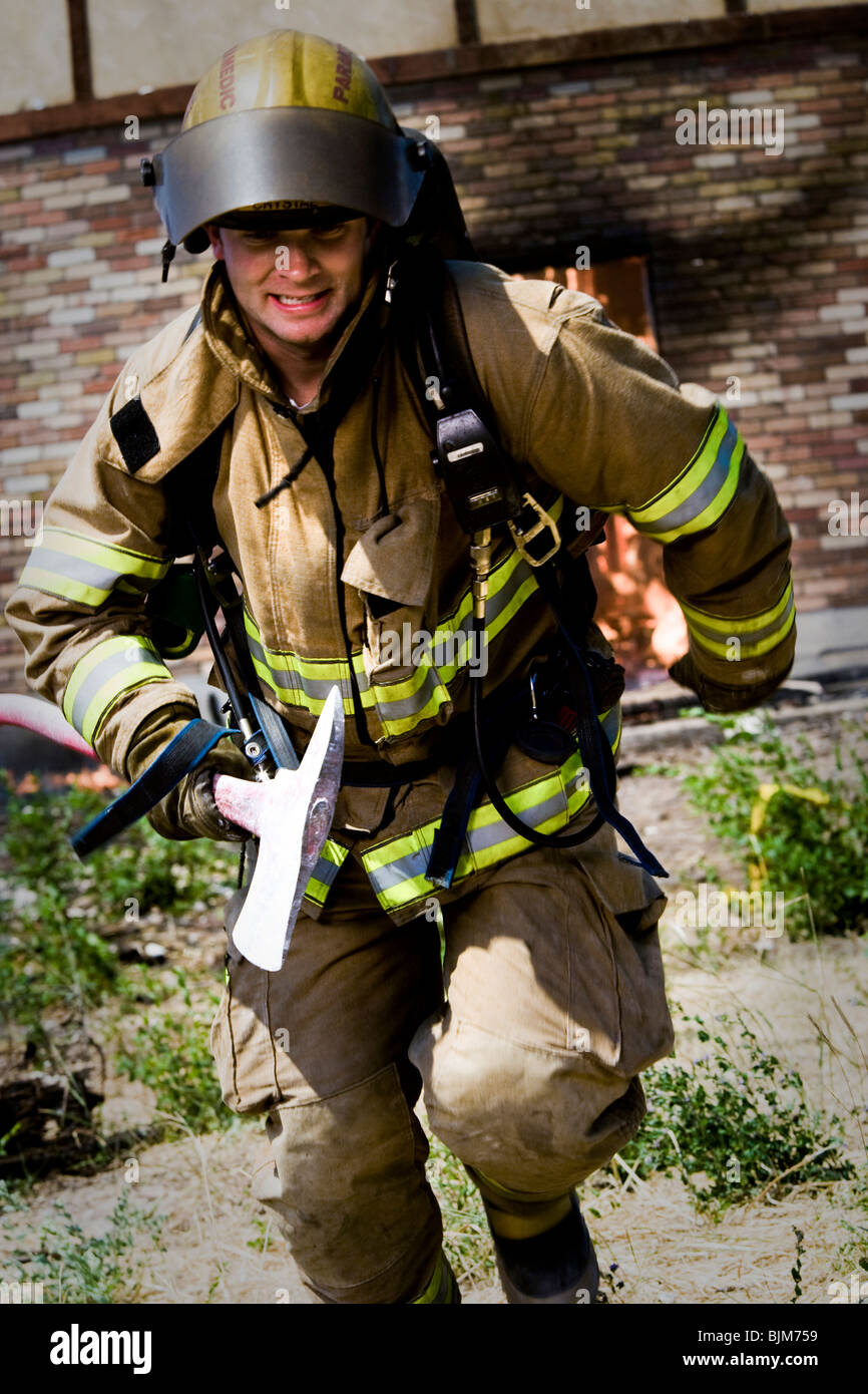 Firefighter with axe running from blaze Stock Photo - Alamy
