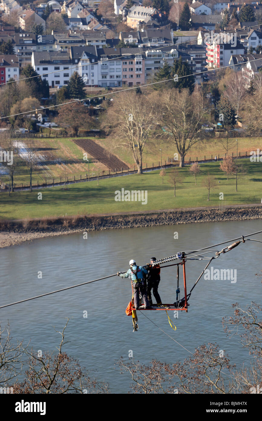 Workers in a safety cage navigate the suspension cable of a cable car ...