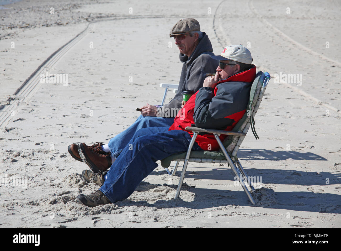 Two men smoking cigars on the beach at Fire Island, New York, on a mild ...