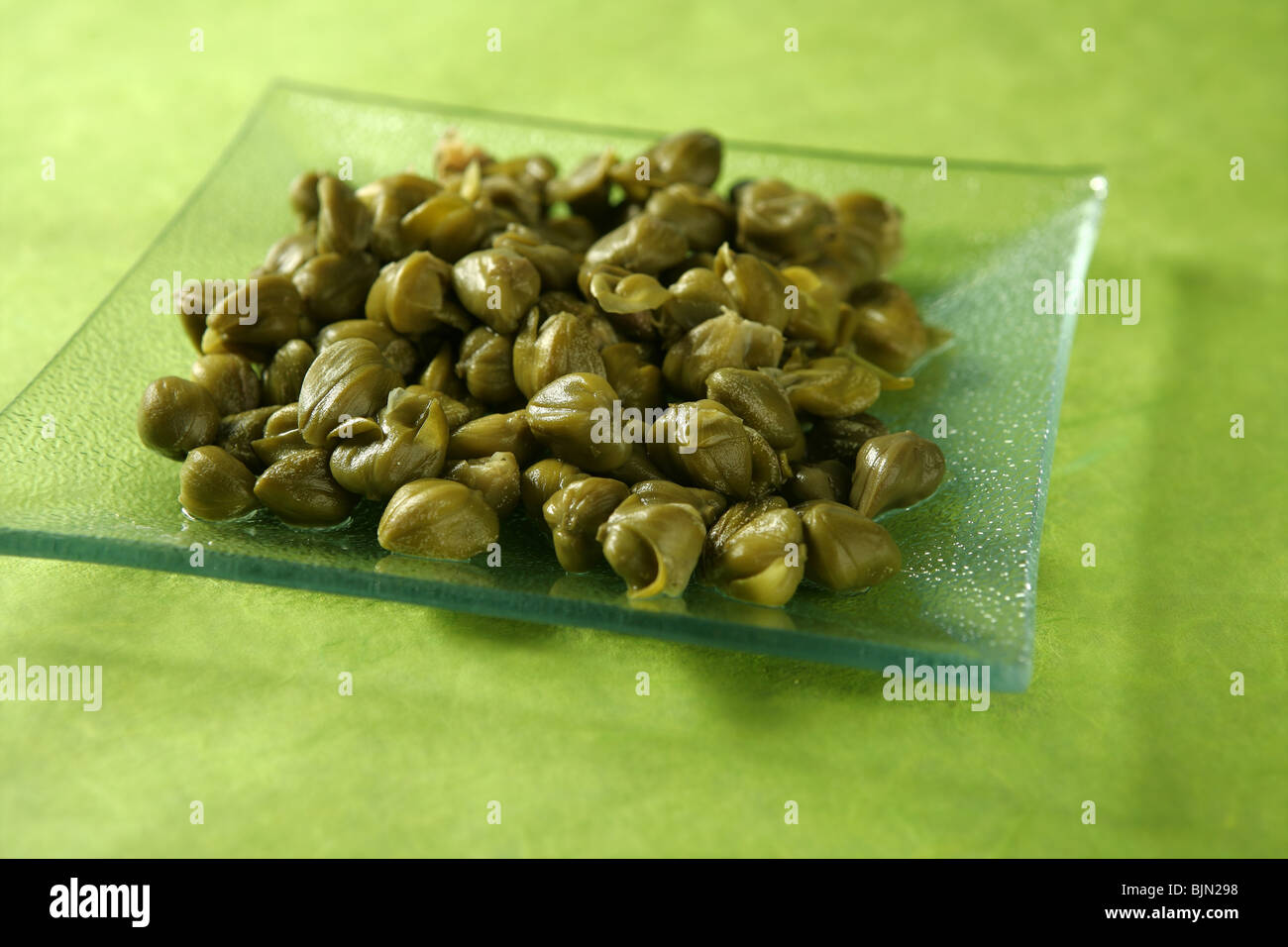 Capers with vinegar snack on a transparent plate, green background ...