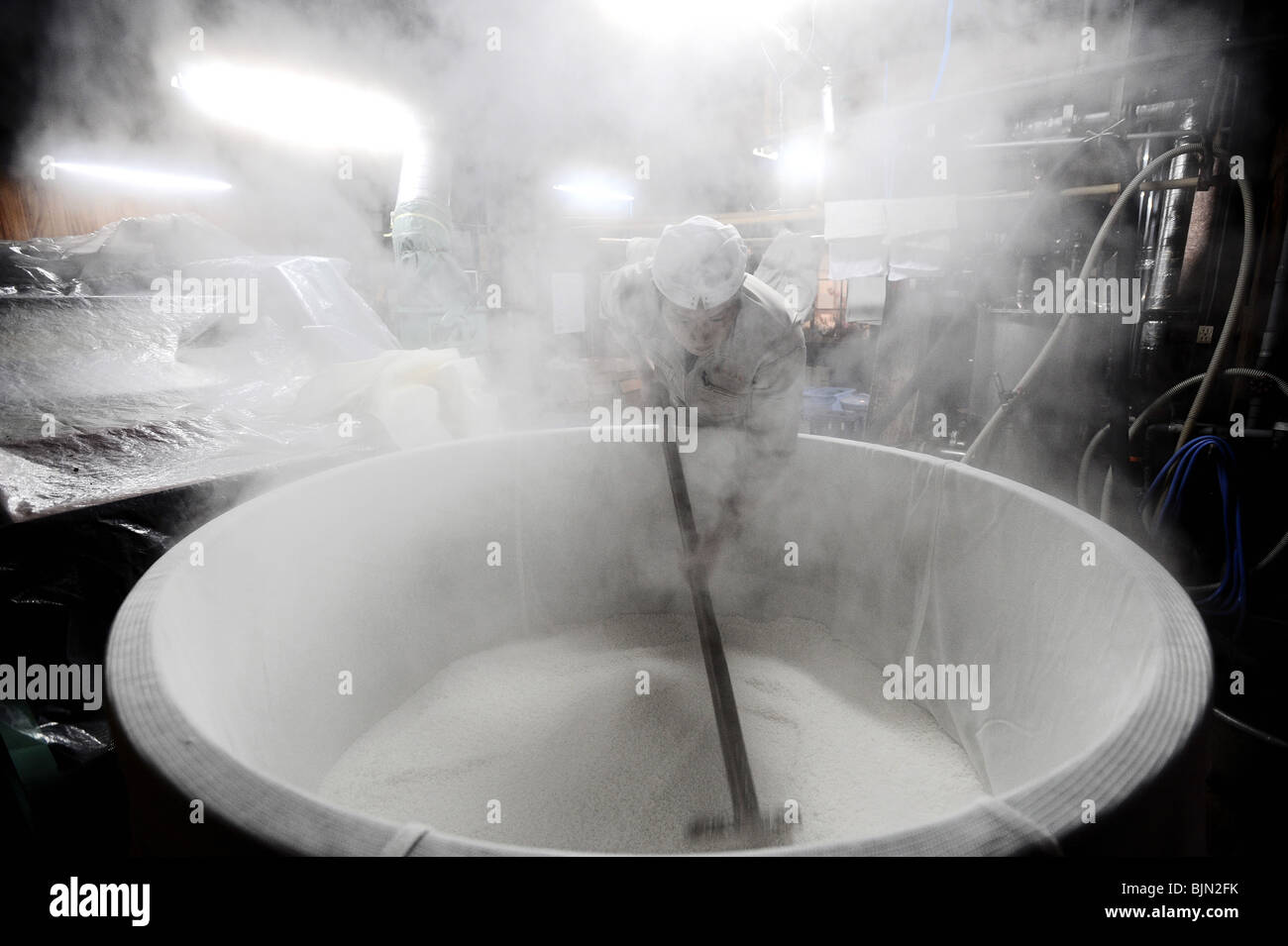 A brewery staff hand mixes steaming rice at a sake brewery in Kyoto ...