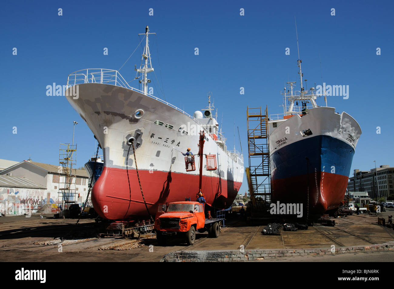 Man in cherry picker painting the hull of a fishing vessel in a ...