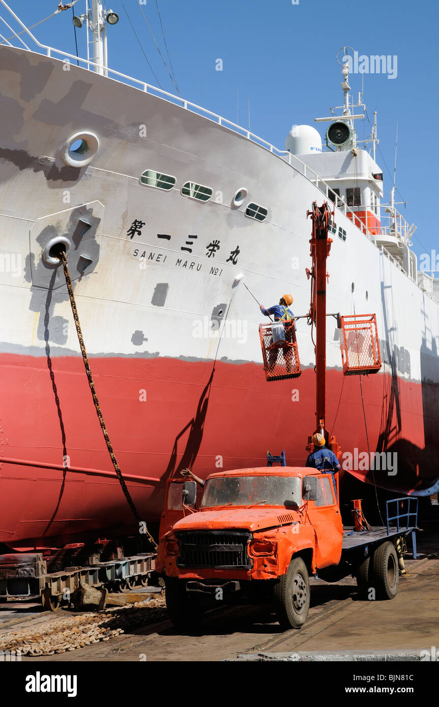 Man in cherry picker painting the hull of a fishing vessel in a ...