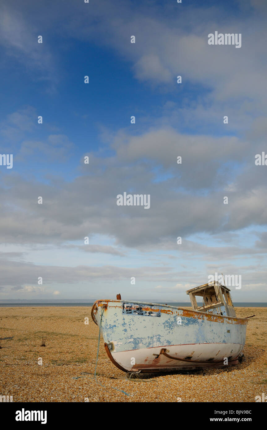 An abandoned fishing boat marooned on a pebbly beach beneath a cloudy ...