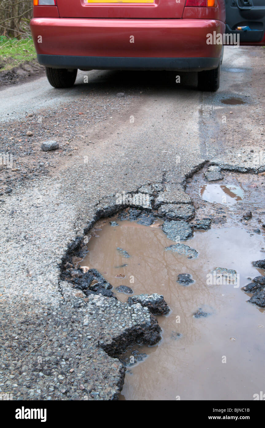 car and wheel beside a pothole left in road by harsh winter weather ...