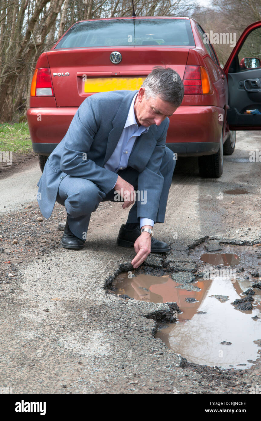 driver with red car inspecting pothole in road caused by severe winter ...