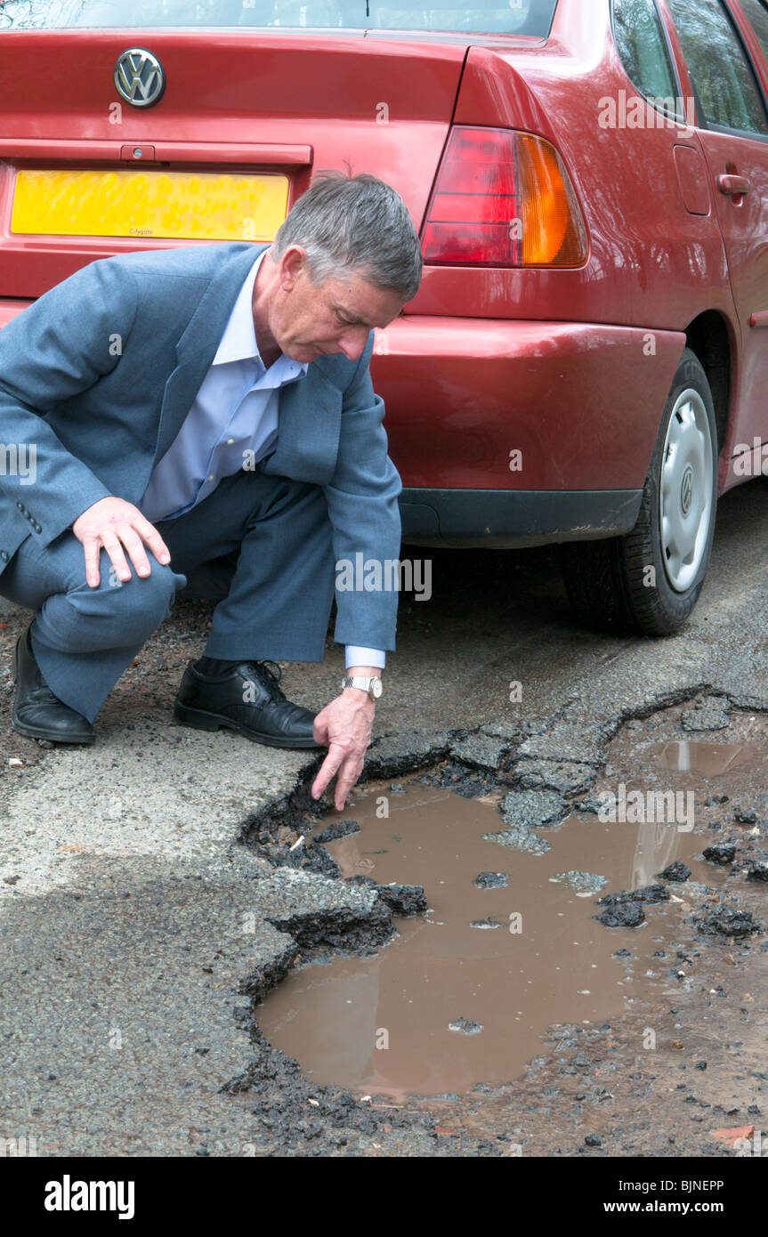 driver with red car inspecting pothole in road caused by severe winter ...