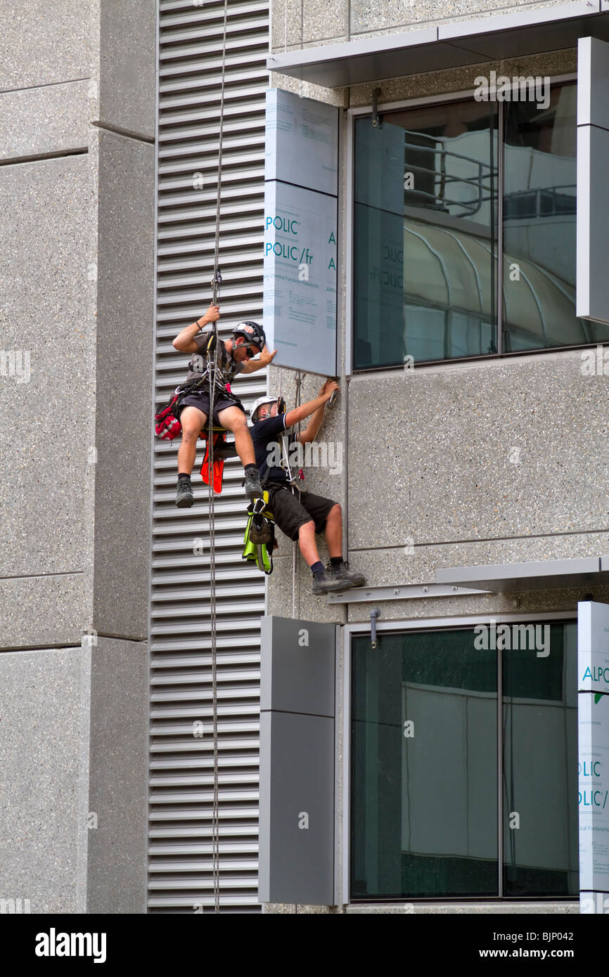 Workers installing sun shade panels on the outside of a highrise ...
