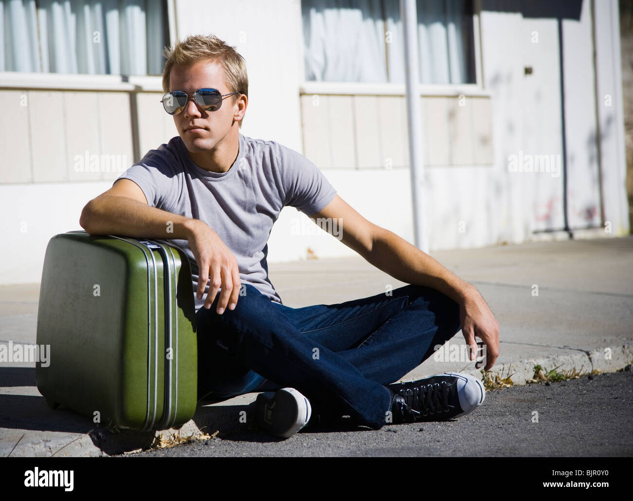Young man sitting with a suitcase Stock Photo - Alamy