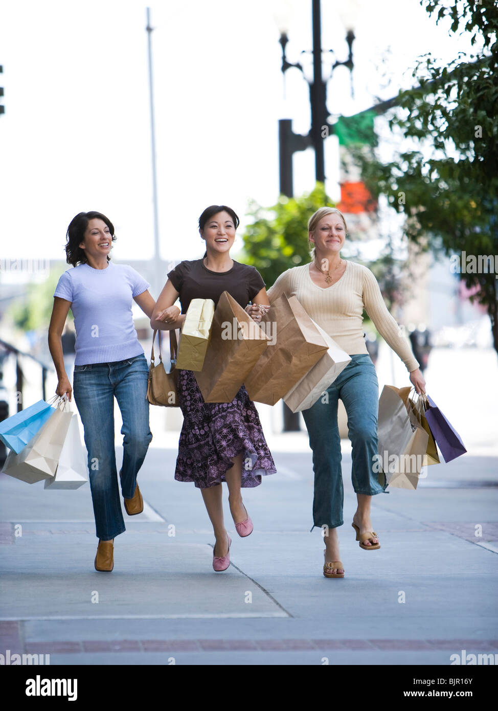 Three girl friends skipping down the street Stock Photo - Alamy