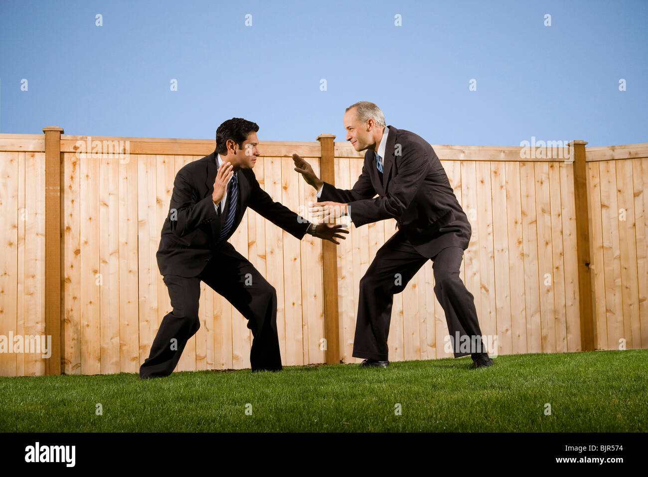 Businessmen in front of a fence playfighting Stock Photo - Alamy