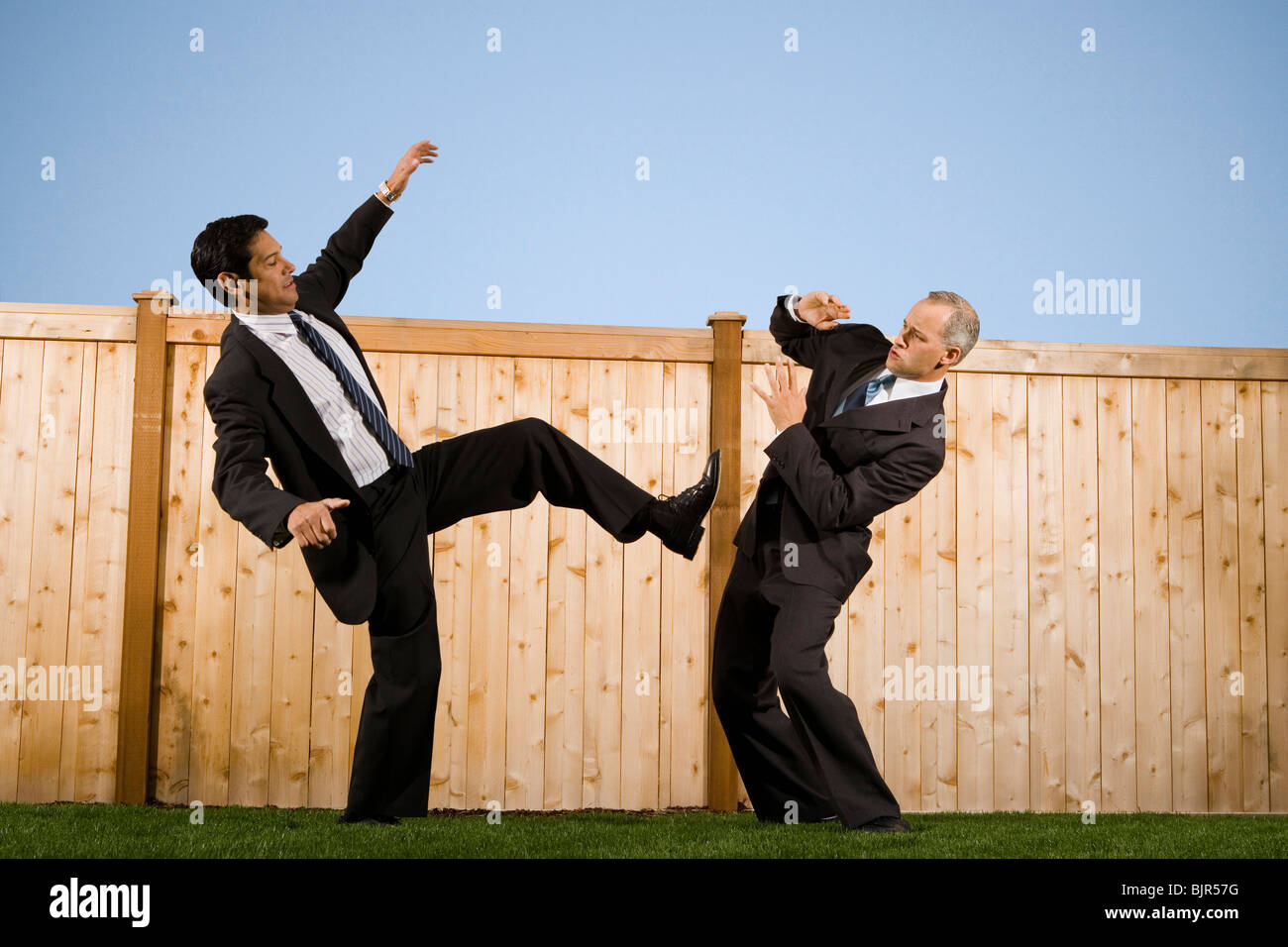 Businessmen in front of a fence playfighting Stock Photo - Alamy
