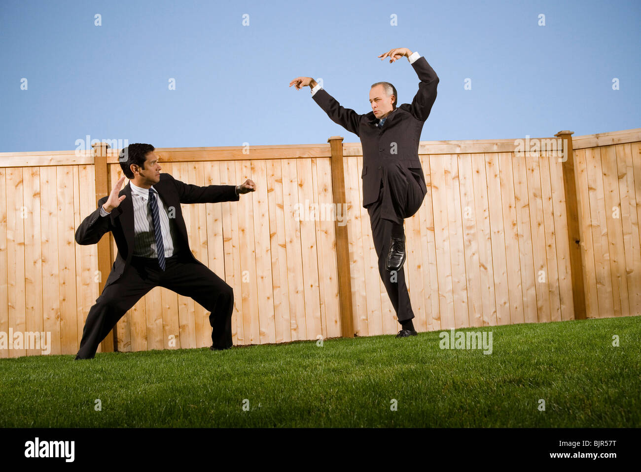 Businessmen in front of a fence playfighting Stock Photo - Alamy