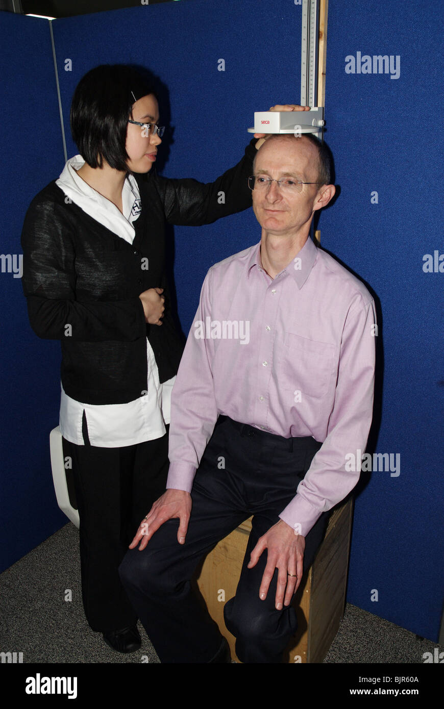 A mature man in a doctors consultant room getting his height tested at ...