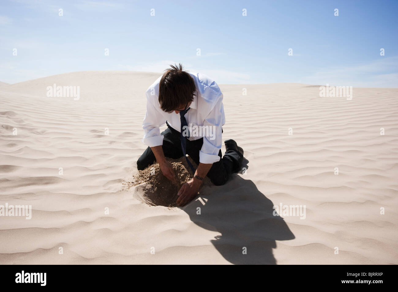 USA, Utah, Little Sahara, mid adult businessman digging hole on desert ...