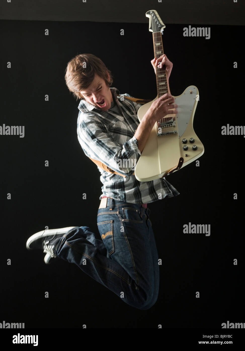 Young man playing electric guitar and jumping Stock Photo - Alamy