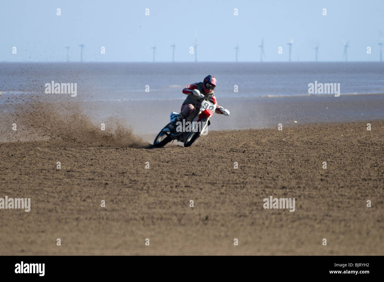 Motor bike sand racing on the beach with wind turbines in the ...