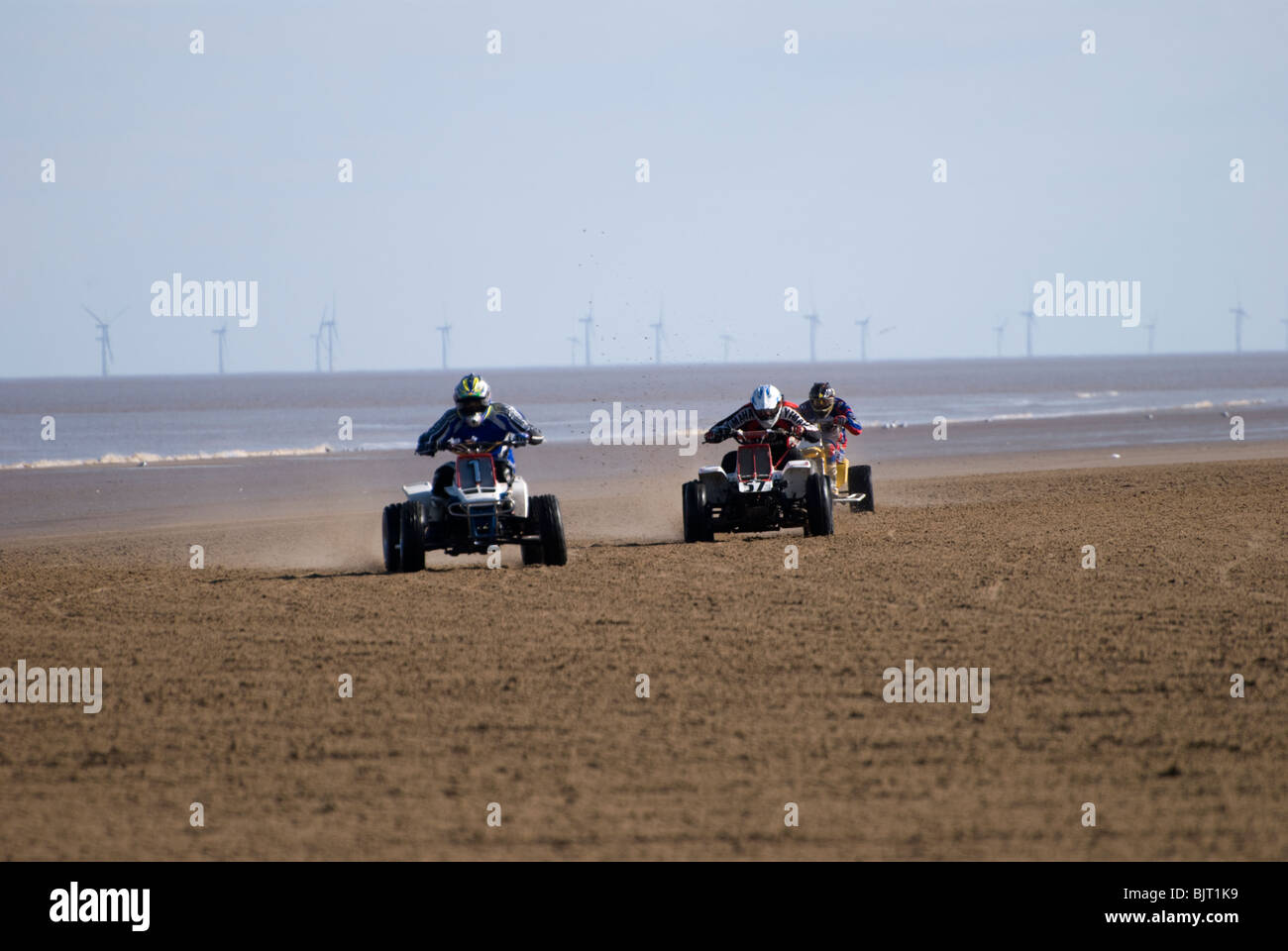 Quad bikes sand racing on the beach with wind turbines in the ...
