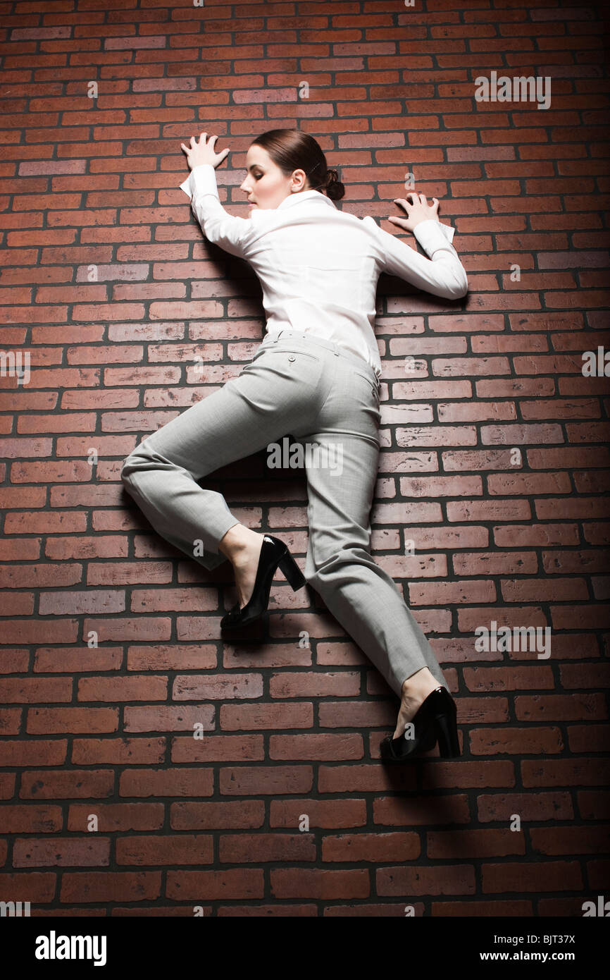 Studio shot of young woman climbing up brick wall Stock Photo - Alamy