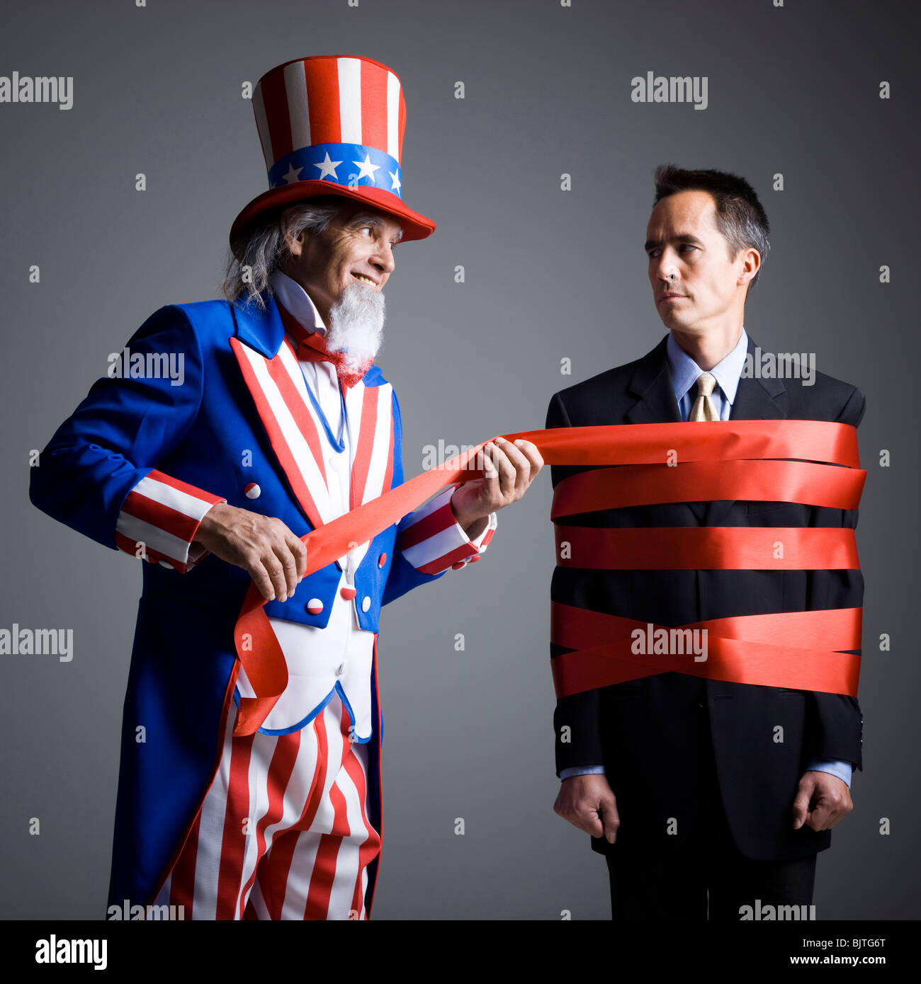 Man in Uncle Sam's costume wrapping other man with ribbon, studio shot ...