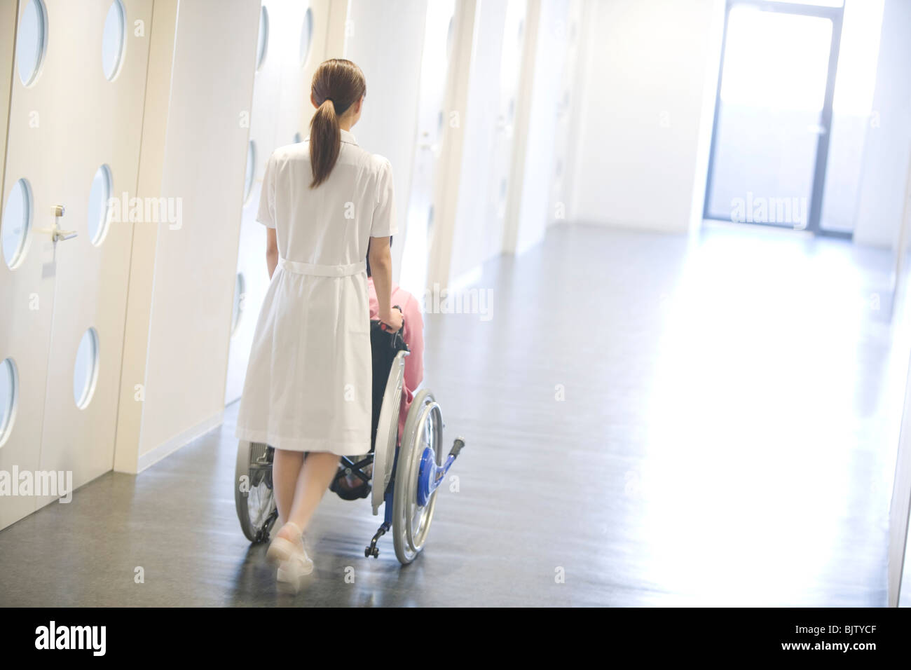 Nurse pushing patient in wheelchair along a corridor Stock Photo - Alamy