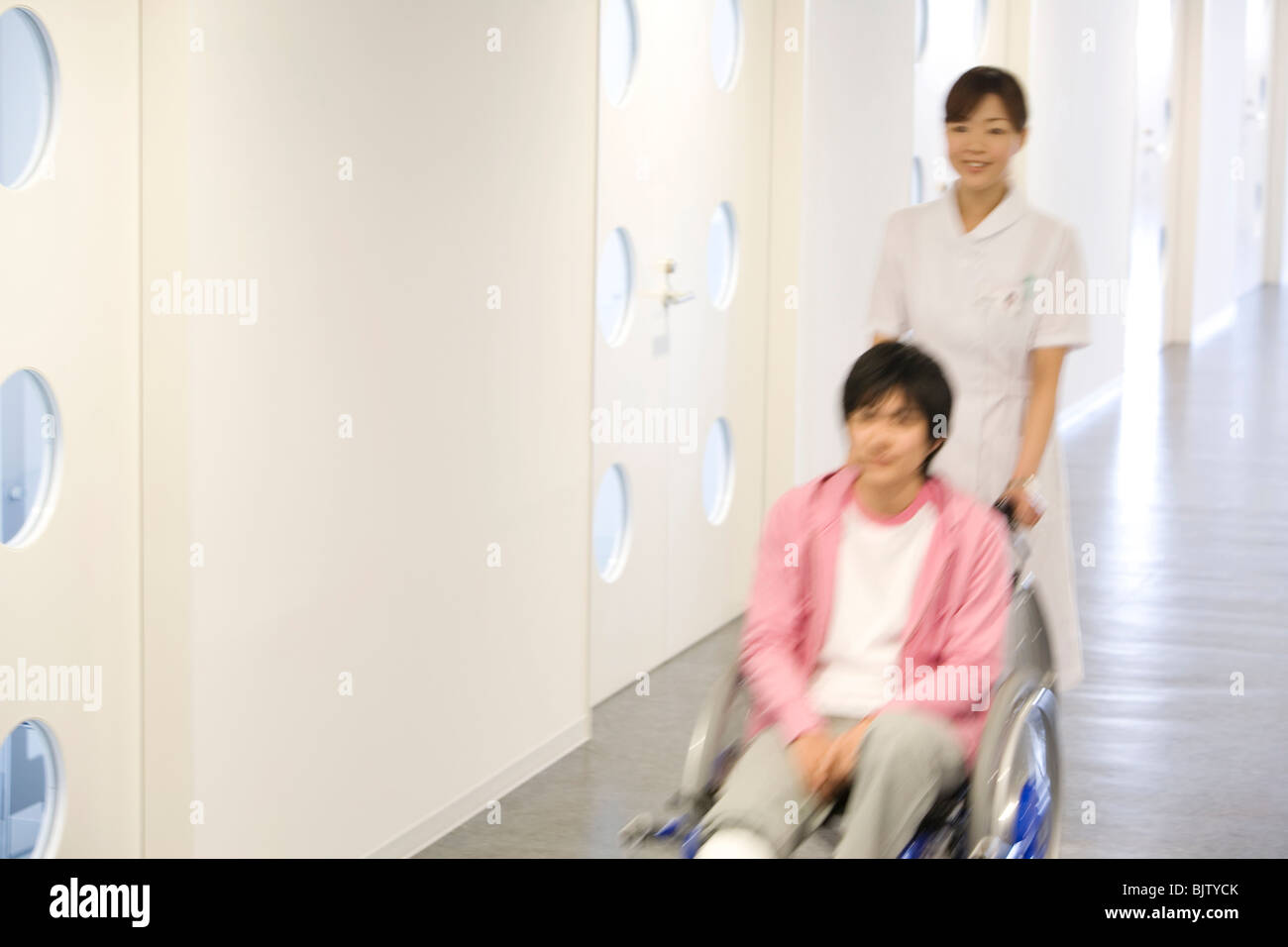 Nurse pushing patient in wheelchair along a corridor Stock Photo - Alamy