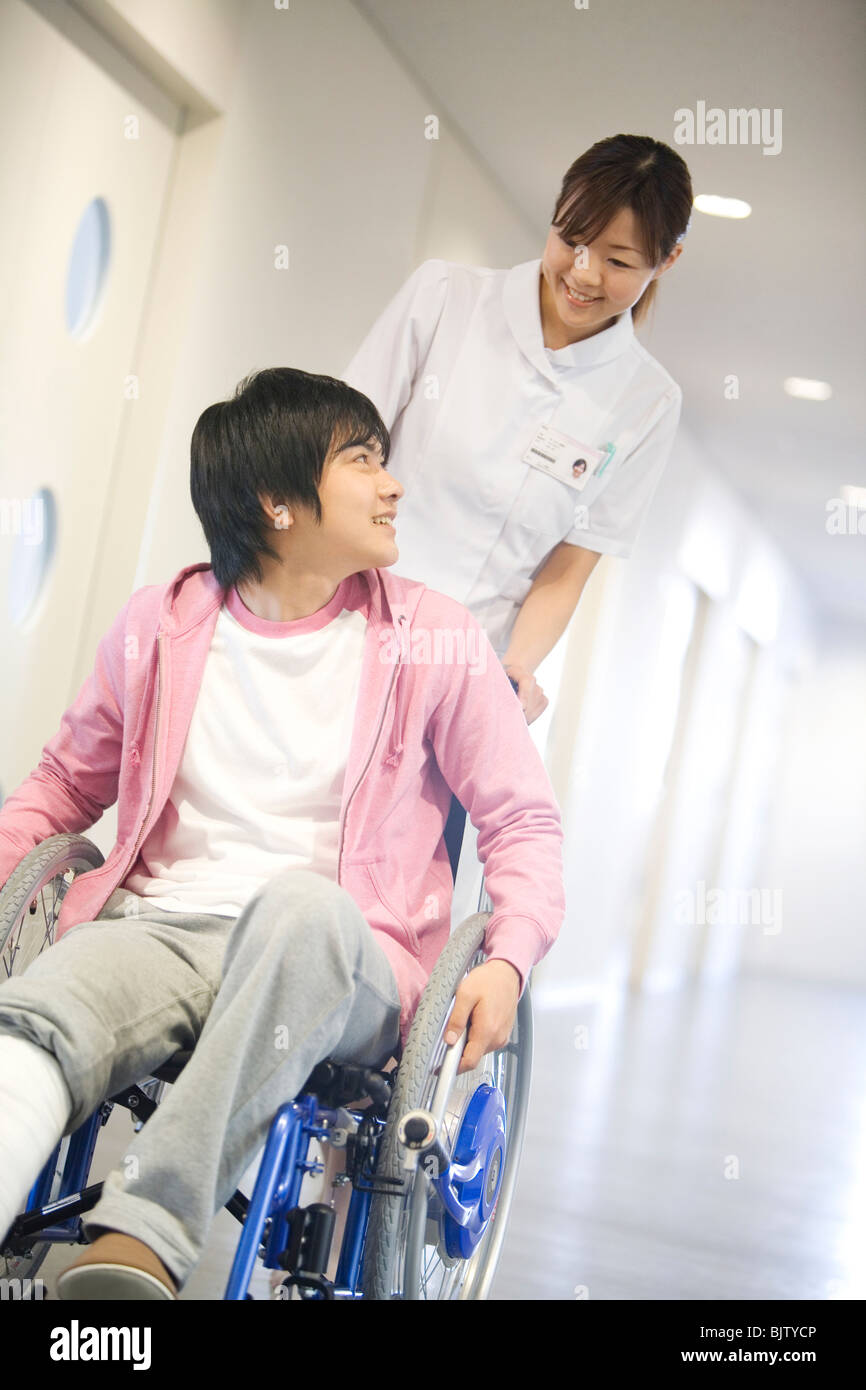 Nurse pushing patient in wheelchair along a corridor Stock Photo - Alamy