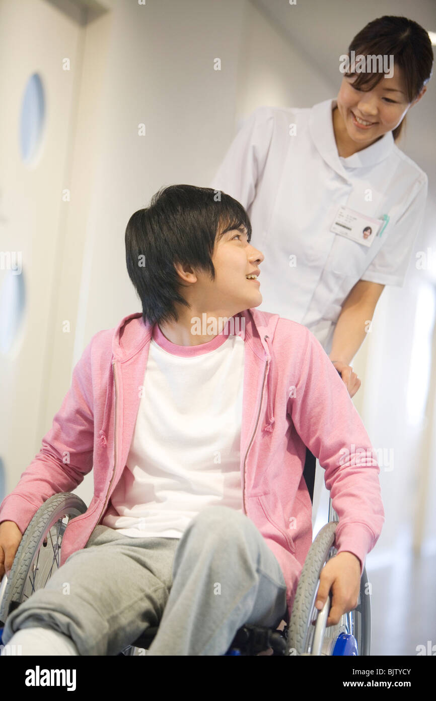 Nurse pushing patient in wheelchair along a corridor Stock Photo - Alamy