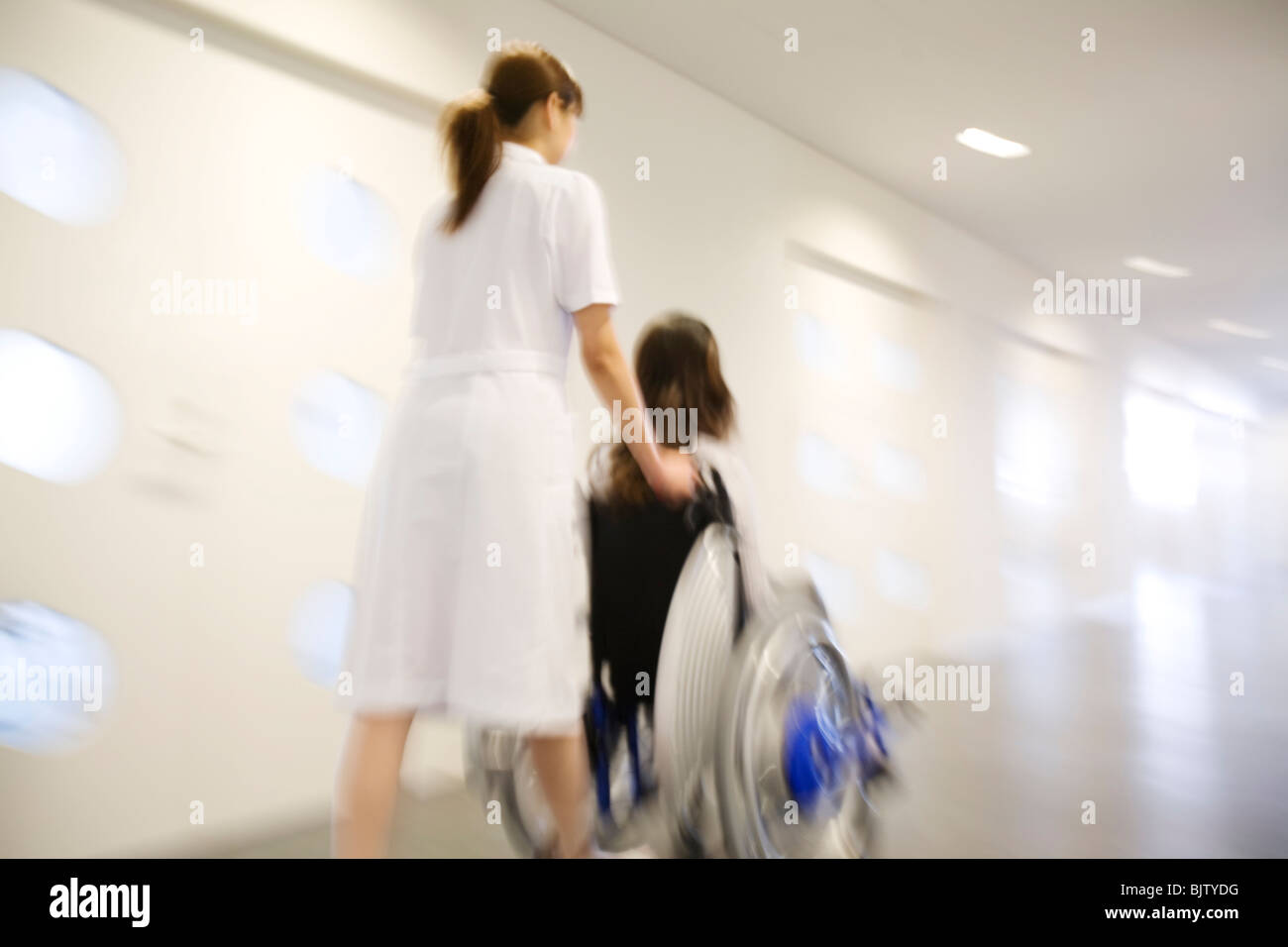 Nurse pushing patient in wheelchair along a corridor Stock Photo - Alamy