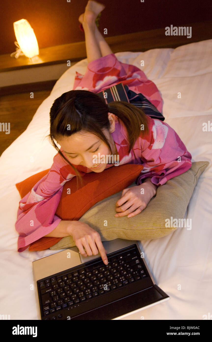 Woman wearing yukata lying on bed using laptop Stock Photo - Alamy
