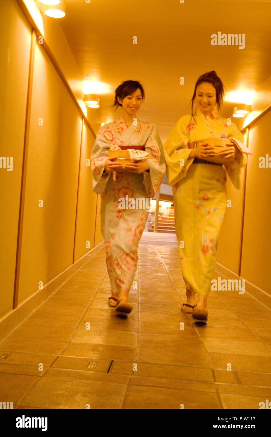 Women wearing yukata walking down a hallway of a health spa carrying ...