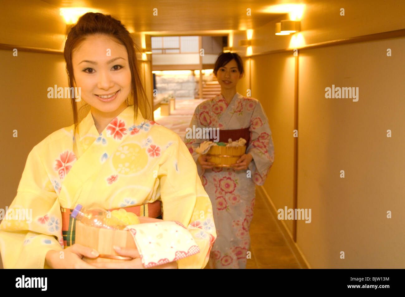 Two women wearing yukata walking through the corridor of a health spa ...