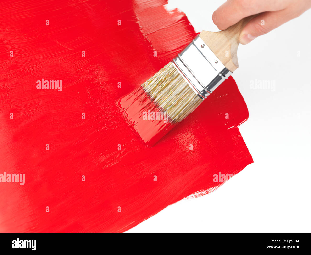 Person holding a paintbrush putting a red coat of paint over white ...