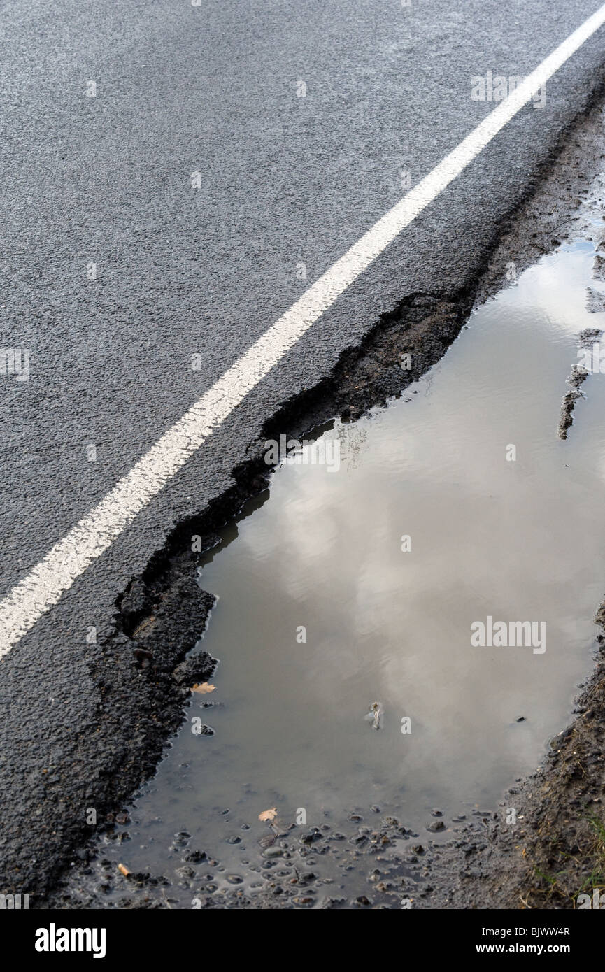 Rain filled Pot hole on side of road with broken tarmac and white line ...