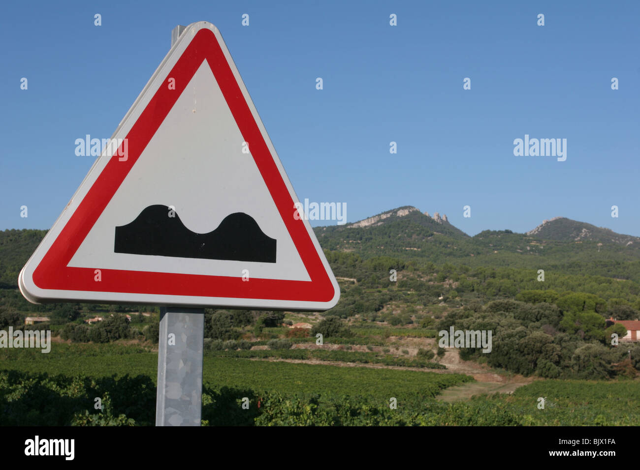 A treet sign indicating a bumpy road in front Les Dentelles, a rock ...
