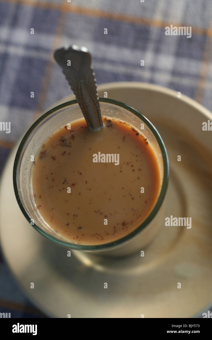a glass of traditional Indian spicy chai tea with spoon on a blue ...