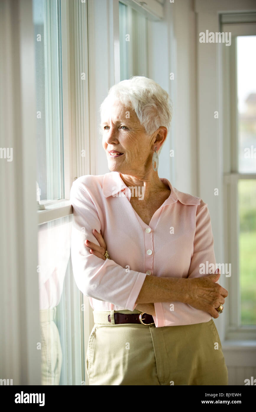 Senior woman leaning against windows gazing out Stock Photo - Alamy