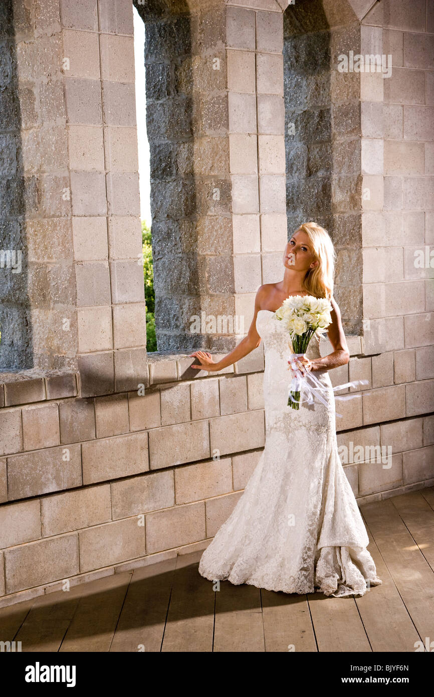 View of young bride standing inside stone building holding bouquet ...