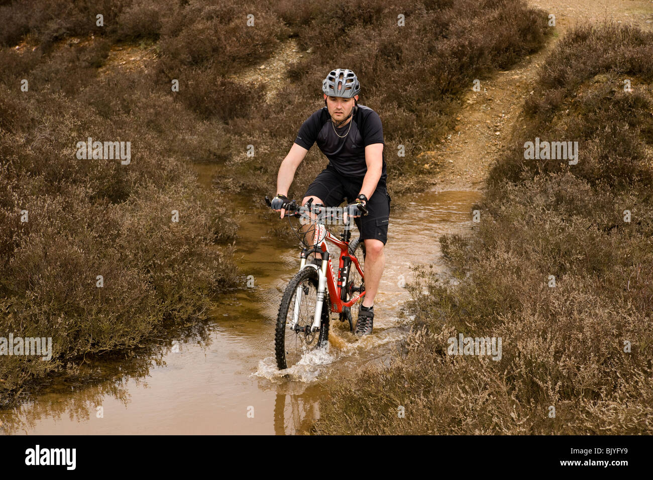 young male mountain biking through rough terrain and water wearing ...