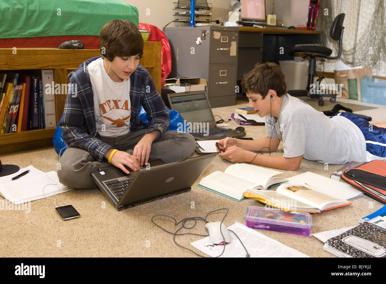 Teen boys in bedroom with laptop computer and textbooks, listening to ...