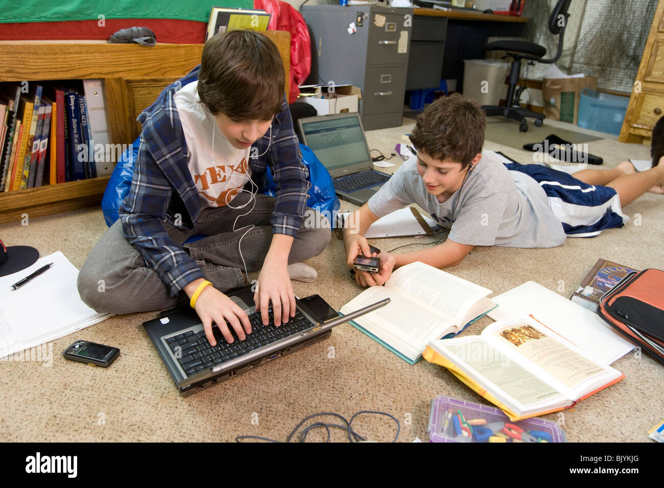 Teen boys in bedroom with laptop computer and textbooks, listening to ...