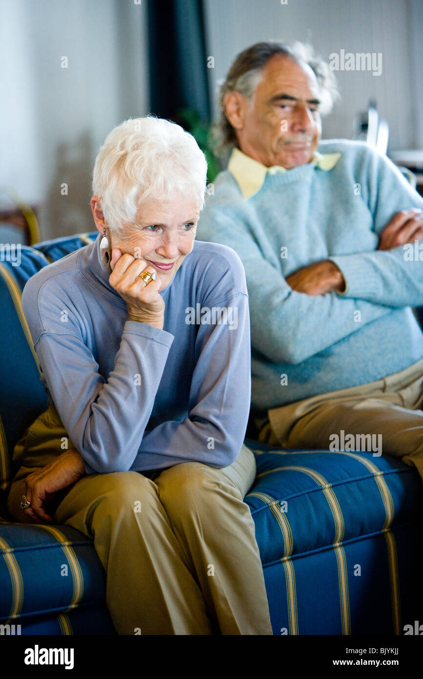 Smiling senior woman sitting on sofa, grumpy man beside Stock Photo - Alamy