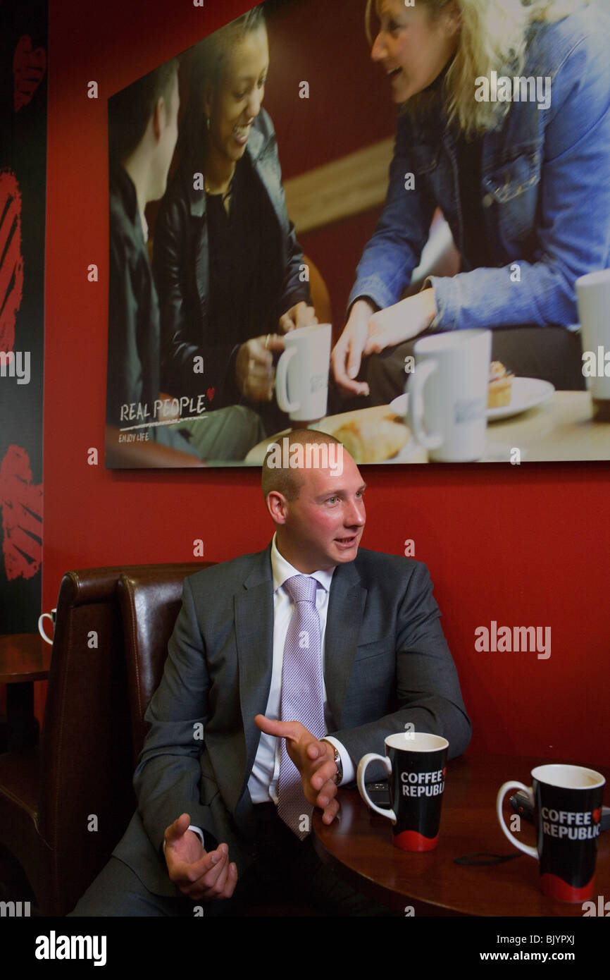 A young man in a smart grey suit chats over coffee in a restaurant ...