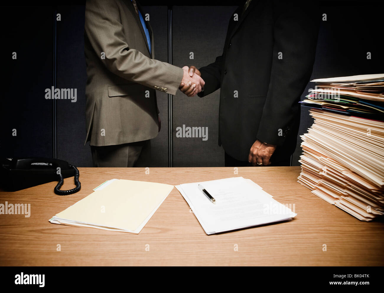 2 businessmen shaking hands at desk Stock Photo - Alamy