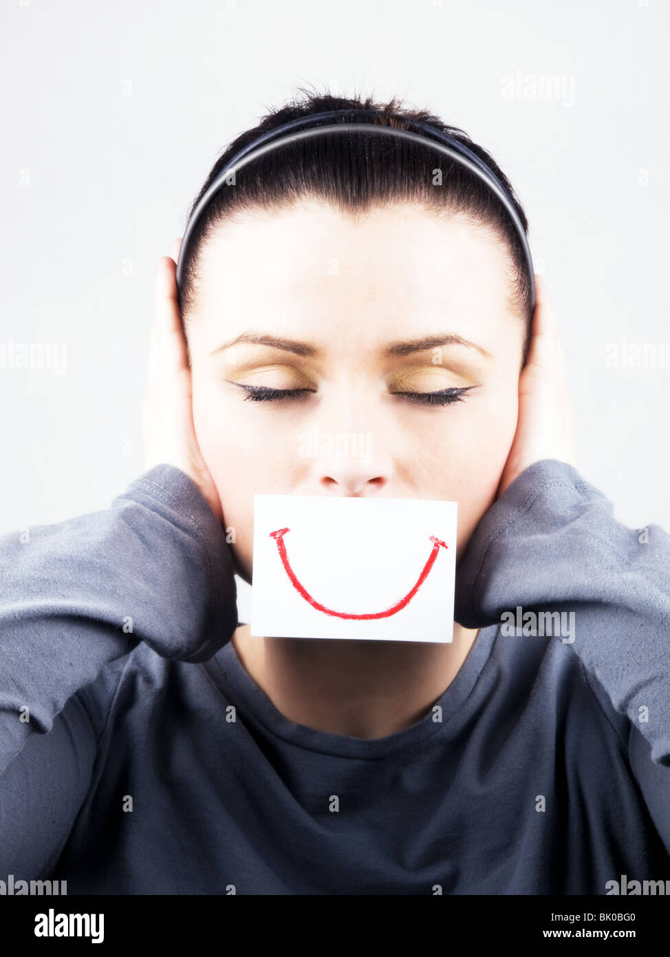 Portrait of beautiful young woman with fake smile. She's cover ears ...