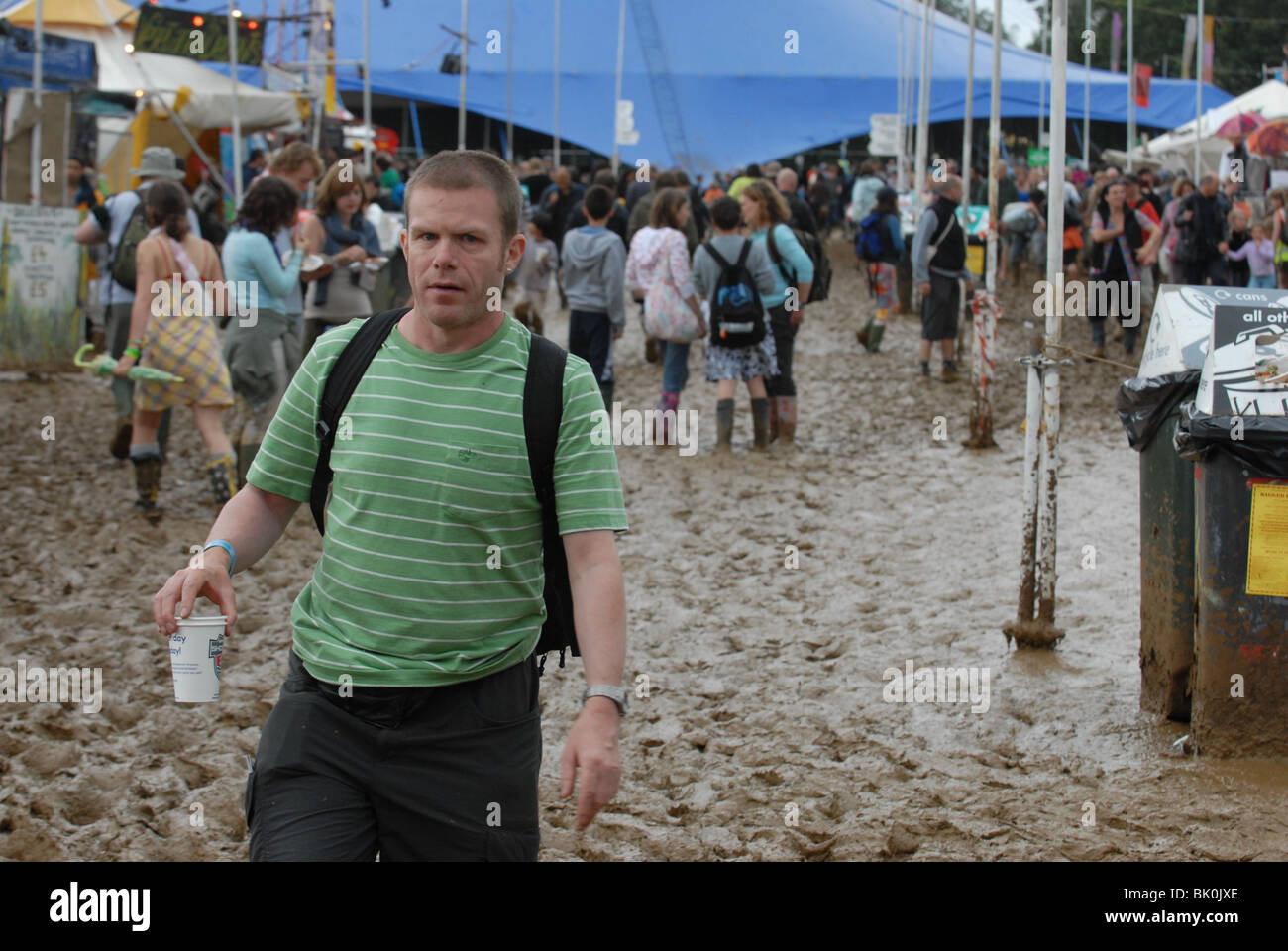 Man carefully carries his drink through the sloppy mud after heavy rain ...
