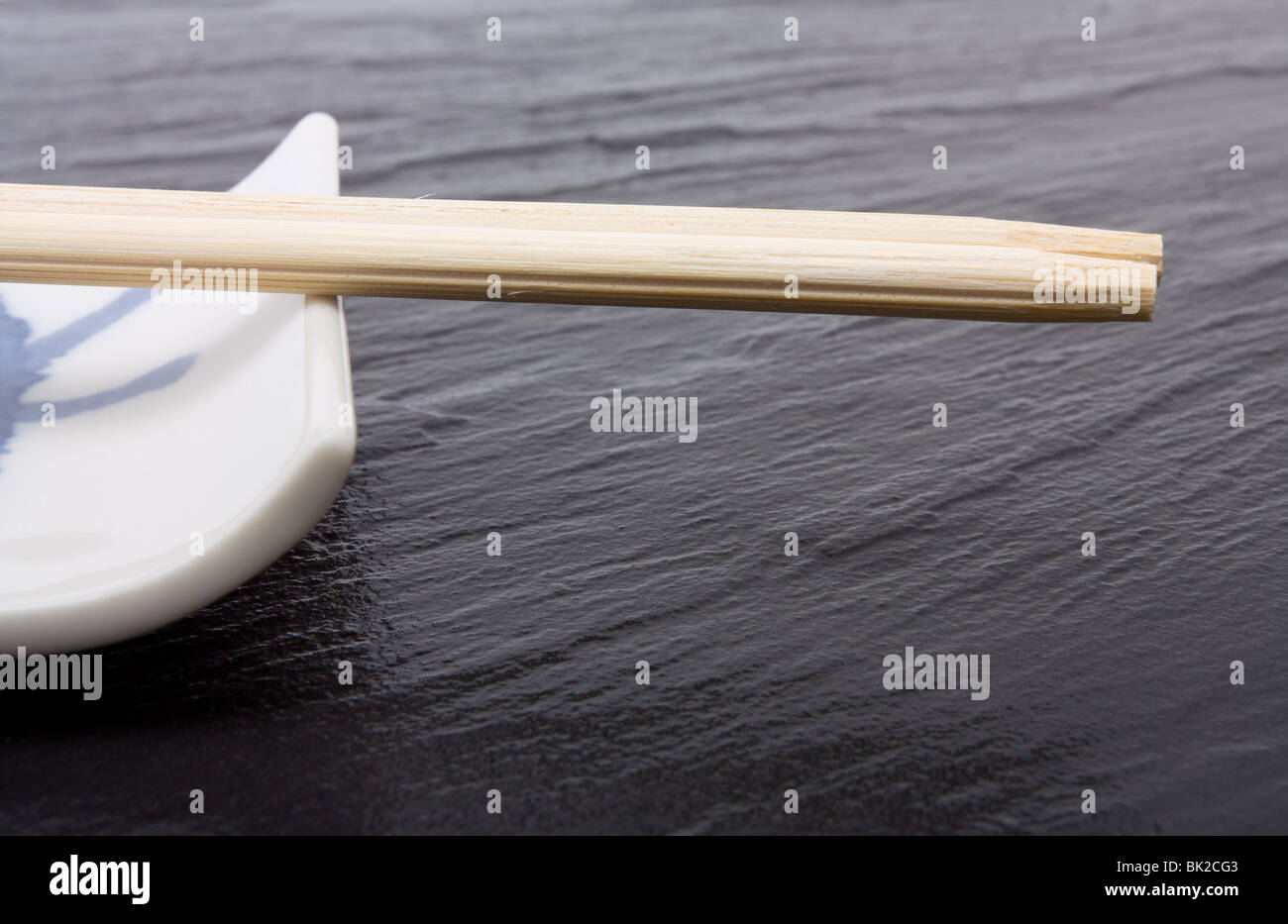 Pair of wood or bamboo Chopsticks arranged on rest against dark slate ...