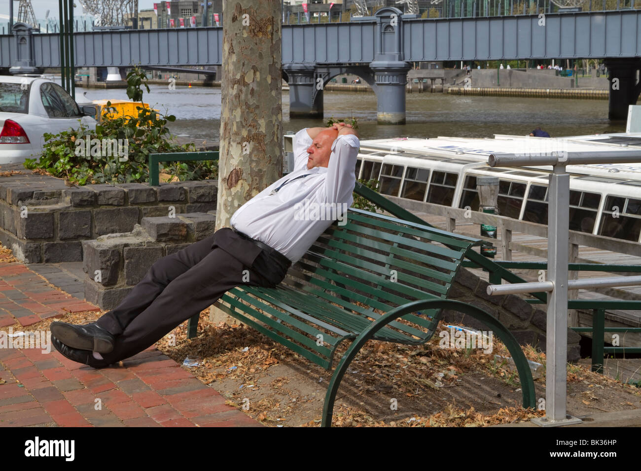 An office worker takes a break relaxing on a bench beside the Yarra ...
