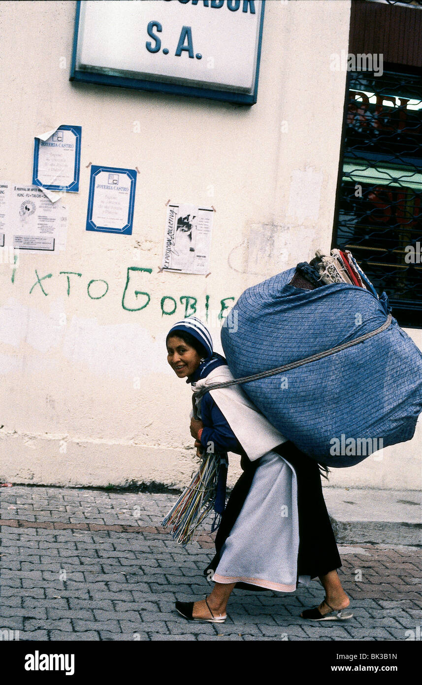 A woman carrying a large bundle of cloth weavings on her back, Ecuador ...